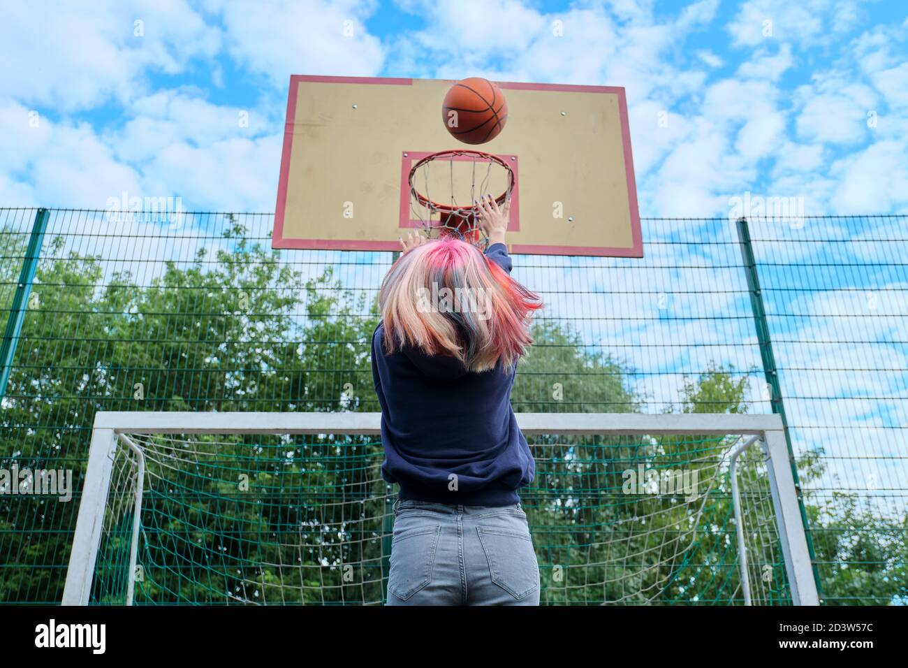Teenager girl jumping with ball playing street basketball, back view ...