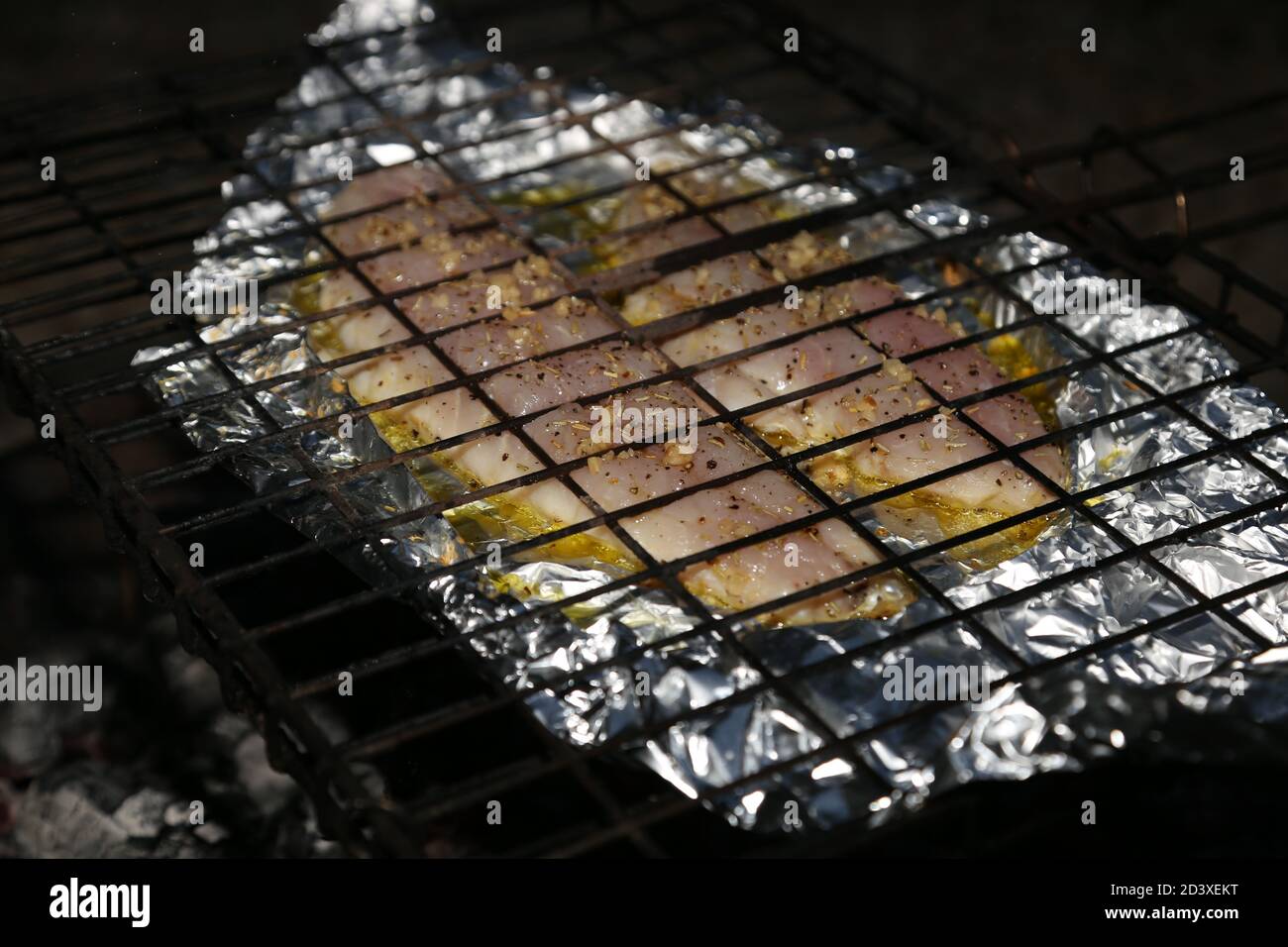 Fish fillets in foil being cooked using a braai grid and hot coals ...