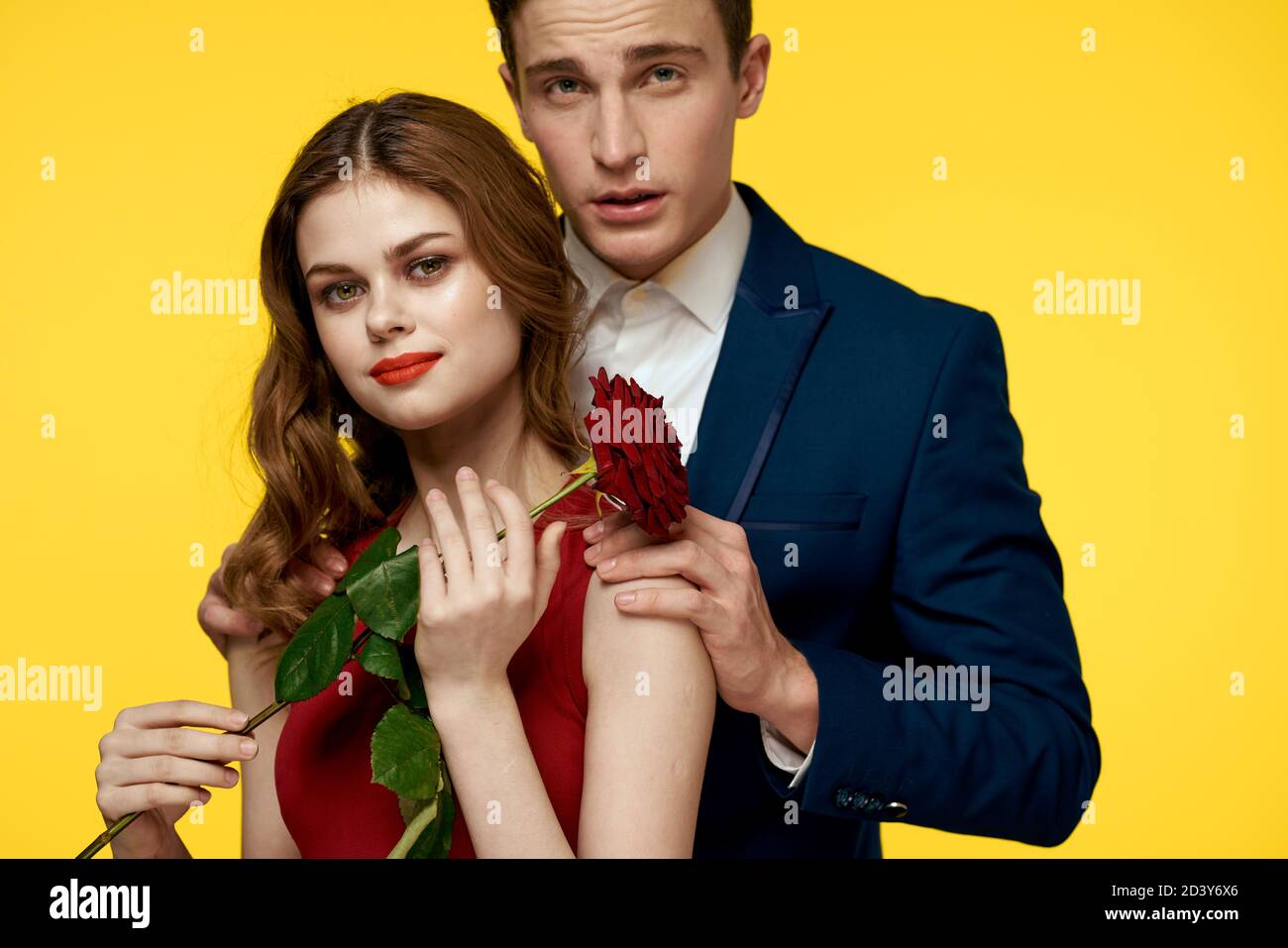 lovers man and woman with a red rose in their hands hugging on a yellow ...