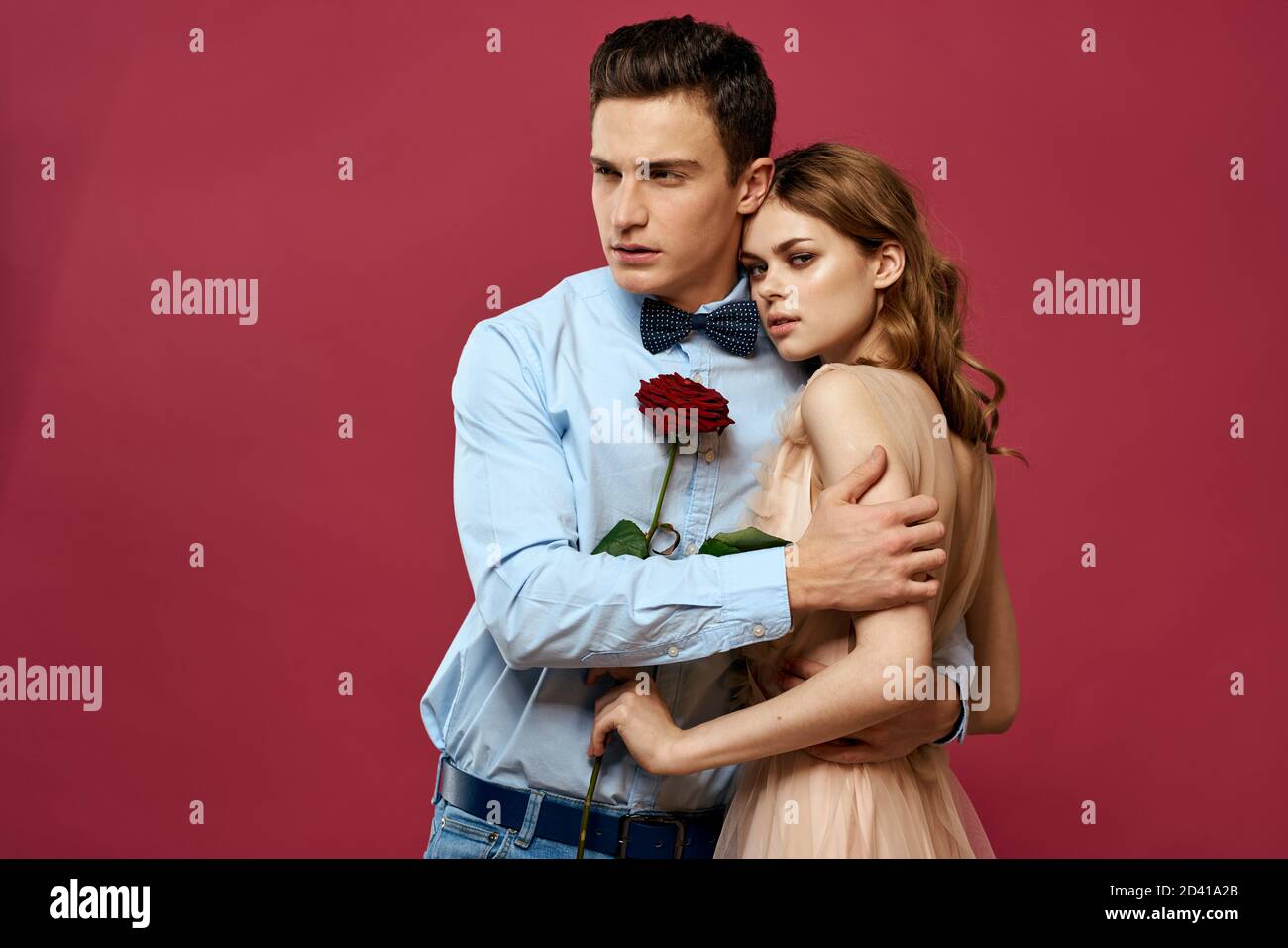 enamored man and woman with a red flower on a pink background hug each ...