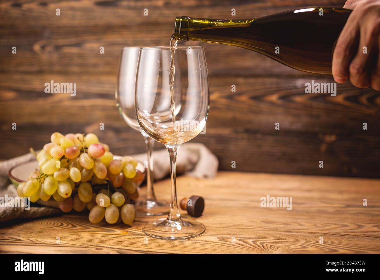 A hand is pouring dry white wine from a bottle into a glass against the ...