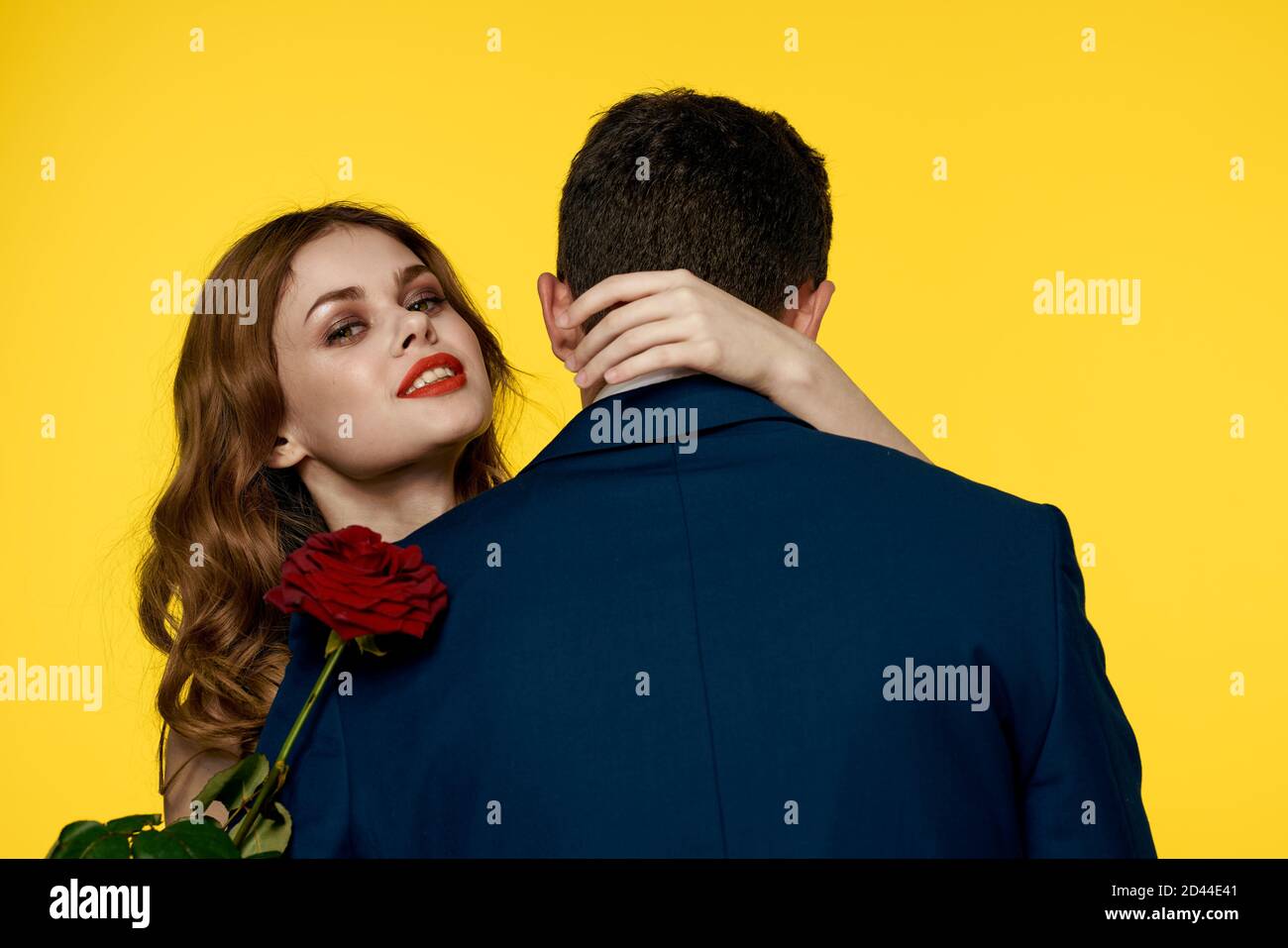 lovers man and woman with a red rose in their hands hugging on a yellow ...