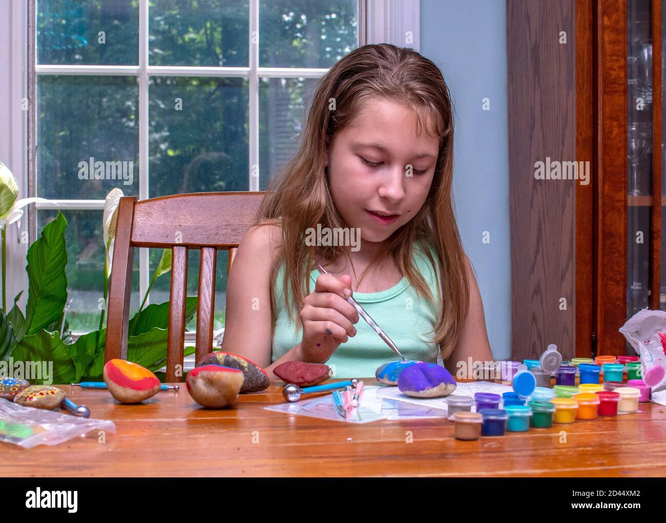 Young girl uses acrylic paint to make colorful artistic painted rocks ...