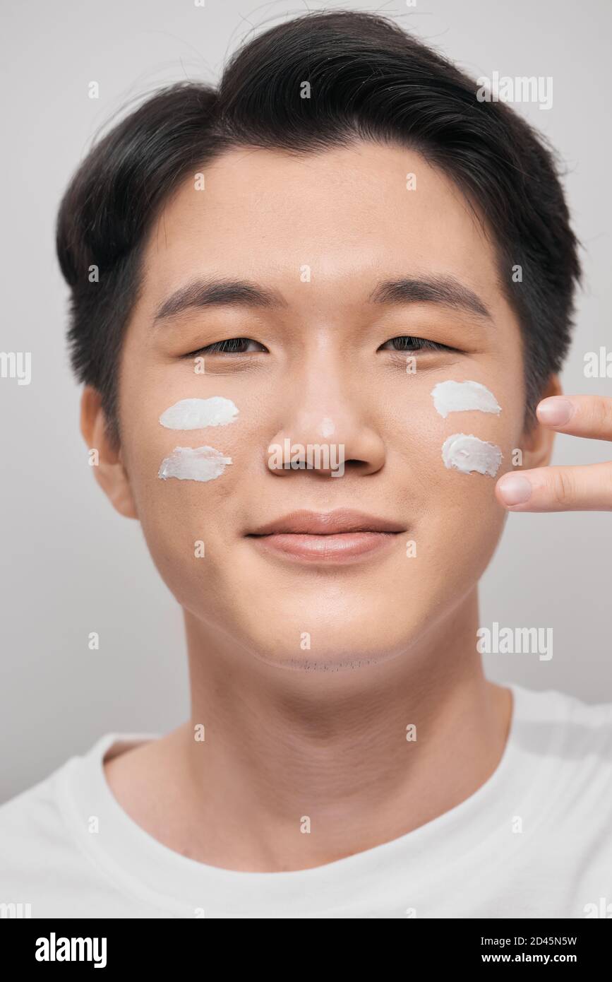 Skin care. Portrait of handsome young man applying cream to his face ...