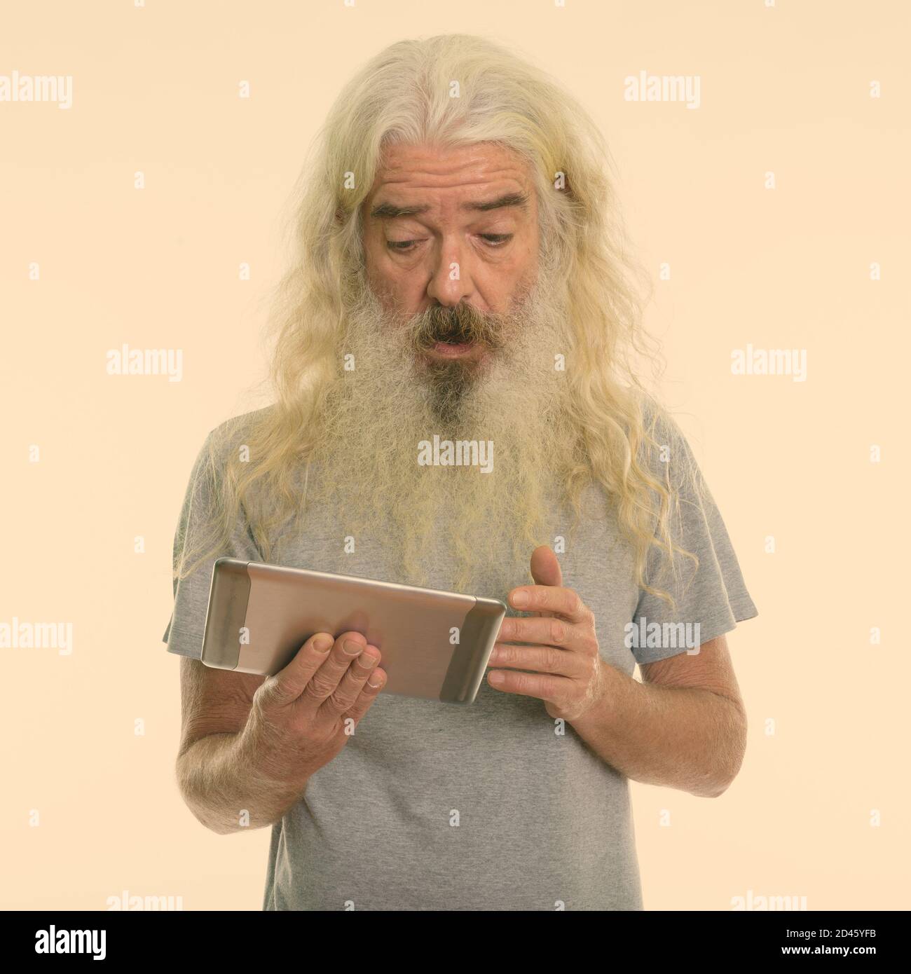 Studio shot of senior bearded man using digital tablet while looking ...