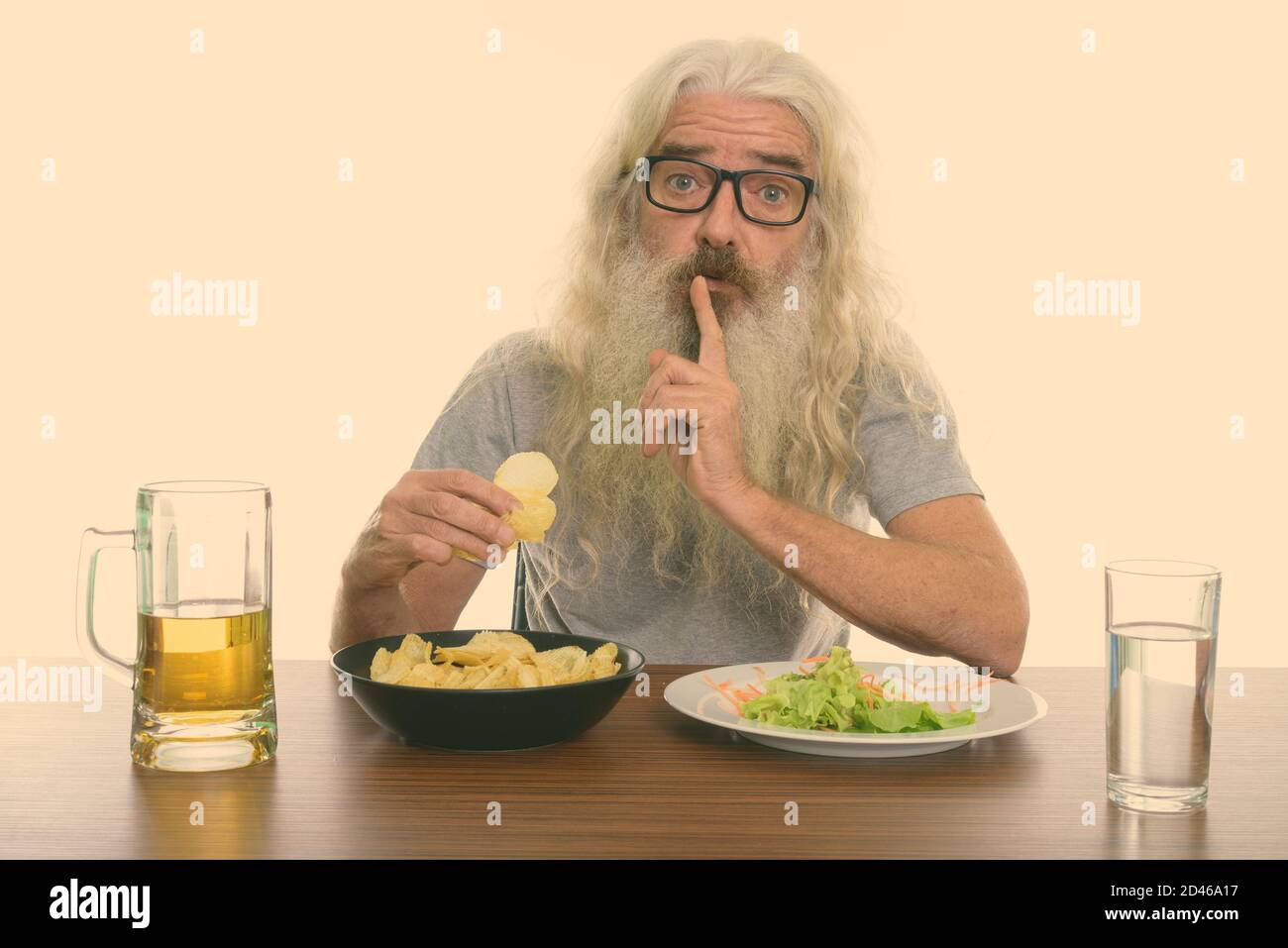 Studio shot of senior bearded man holding potato chips while shushing ...