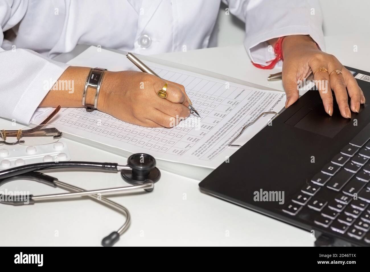 Indian doctor referring her laptop while writing a medical prescription ...