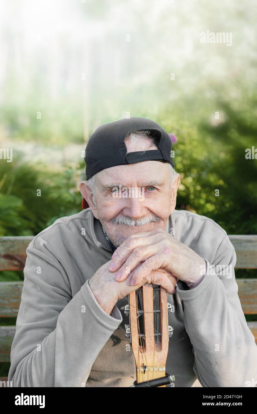 old mustachioed male rocker sits with an acoustic guitar outdoors in ...