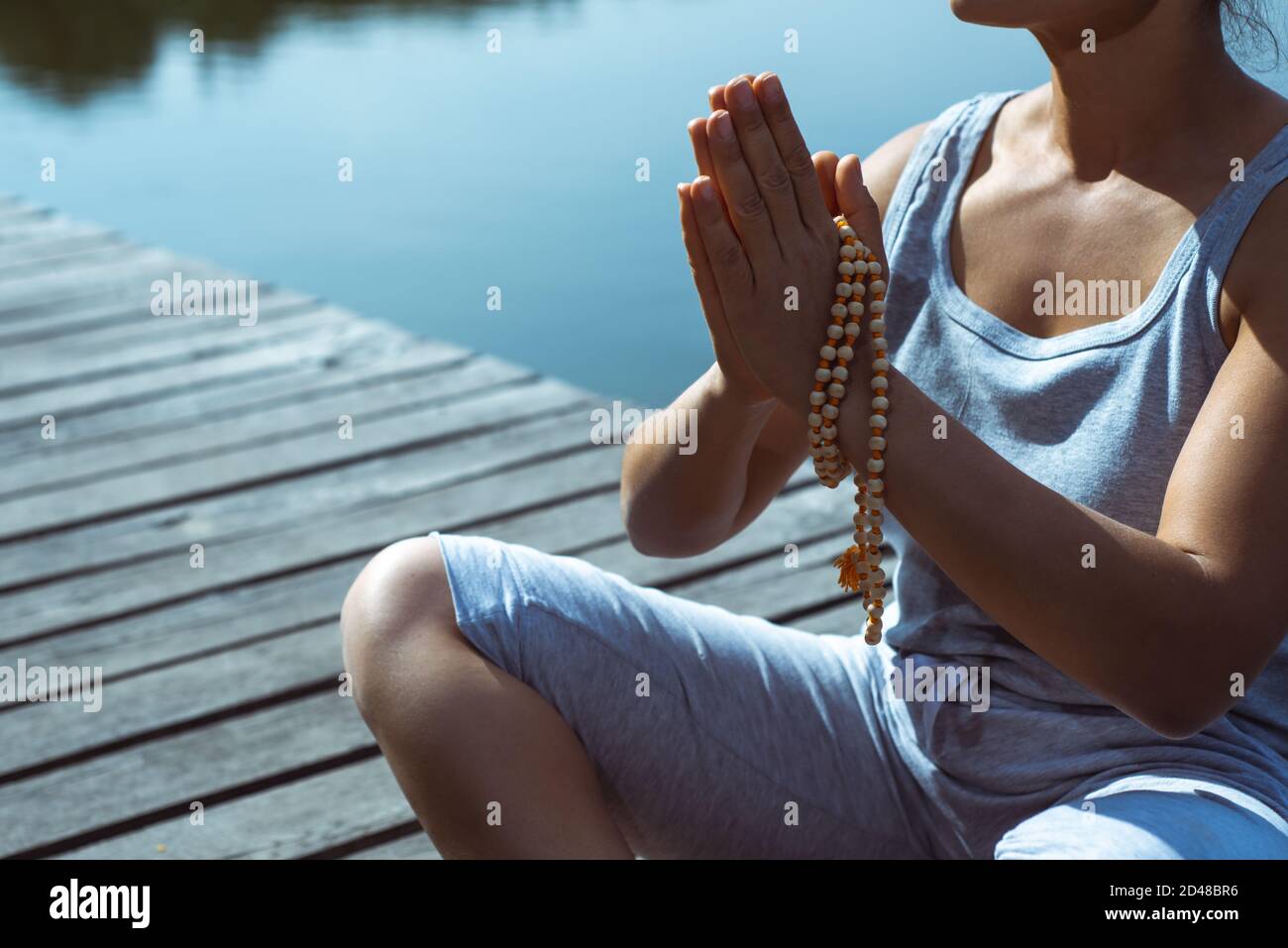 The young woman on a wooden pier sits in a lotus position with her ...