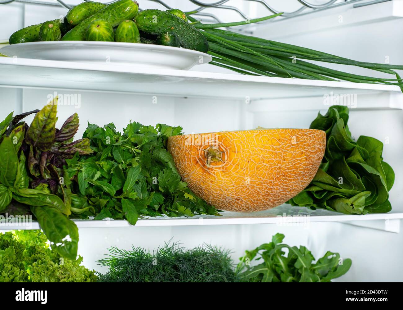 Fridge contents with green vegetables and melons in the center of the ...