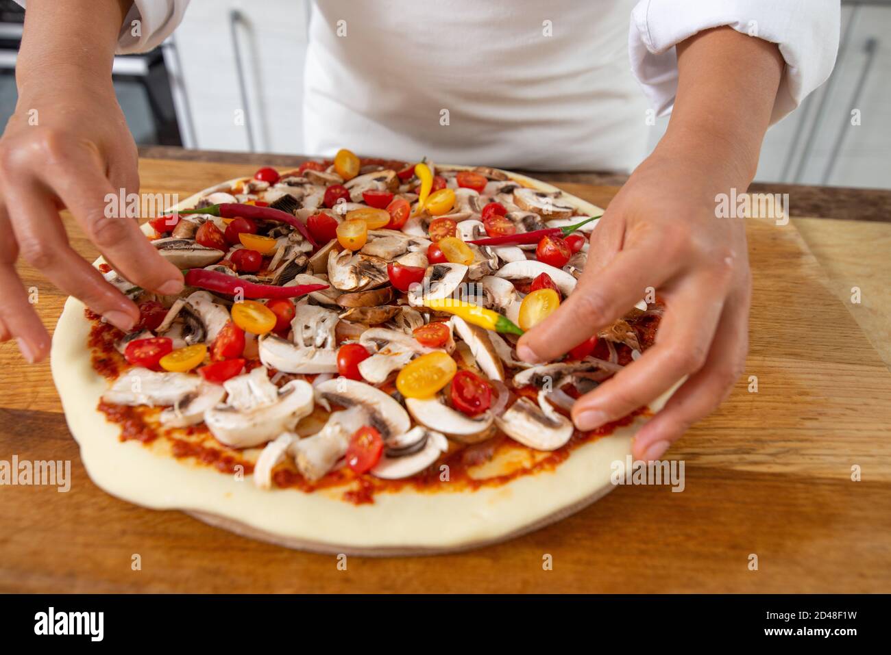 The view of the hands of the chef adding hot peppers to the pizza ...