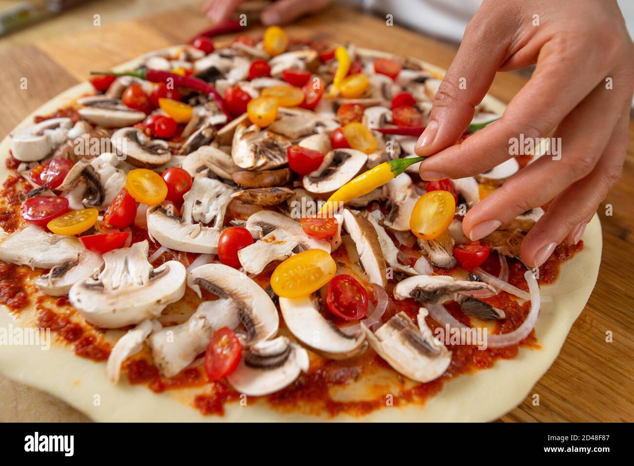 The view of the hands of the chef adding hot peppers to the pizza ...