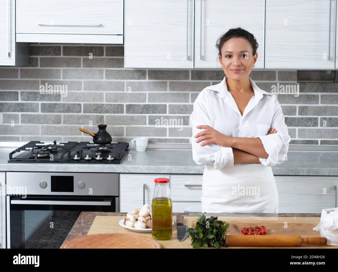 The young woman cook stands in the kitchen in front of the table with ...