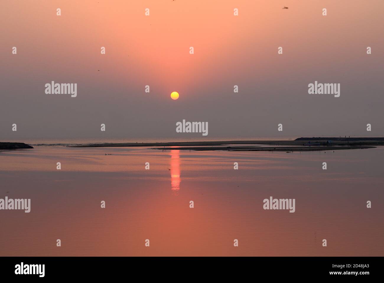 The bright round full sun rises from the ocean at the confluence of the ...