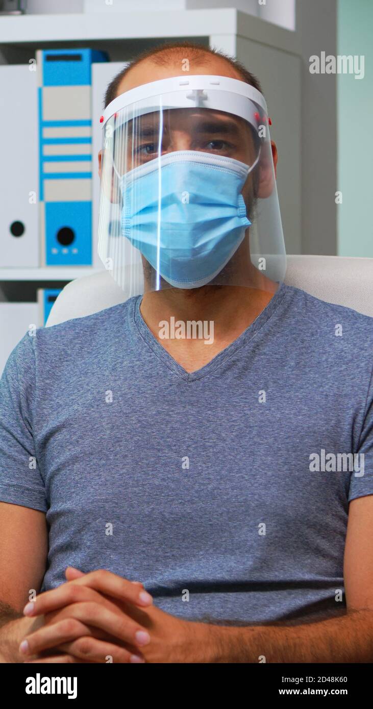 Busy employee wearing mask and visor in work place, typing and looking ...