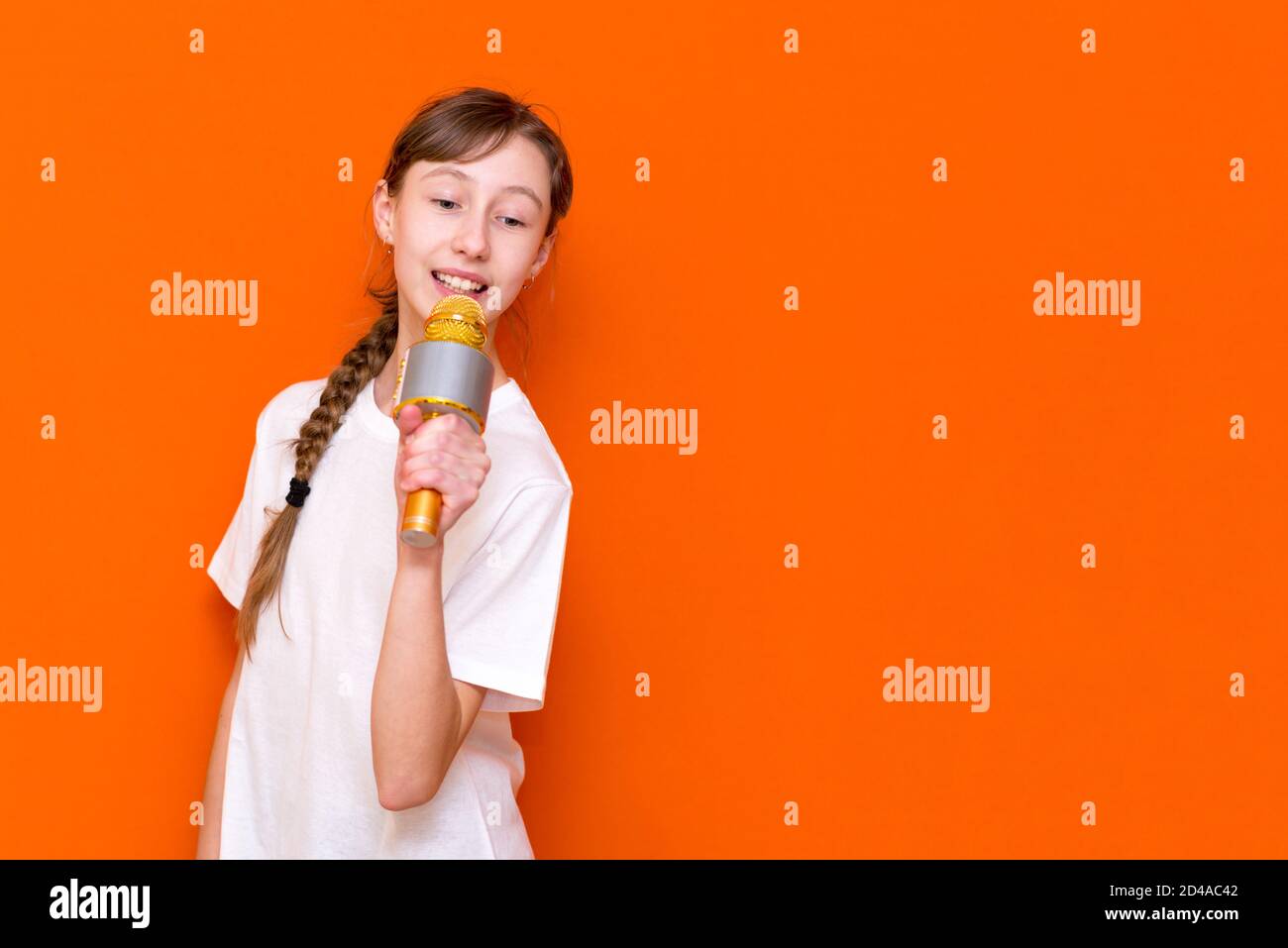Happy young beautiful girl singing with microphone on orange studio ...