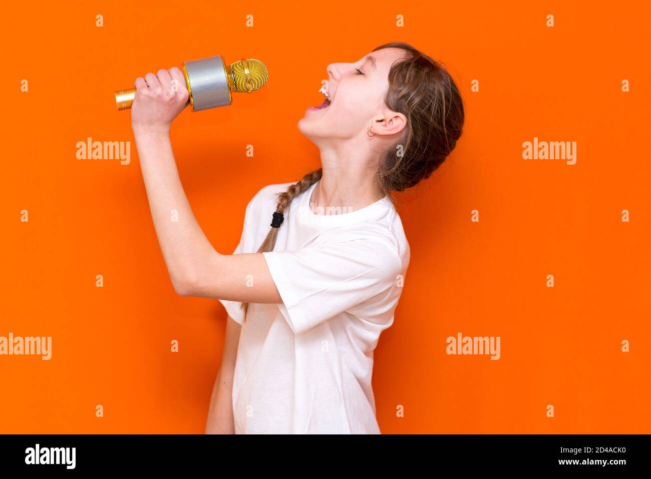 Side view Happy young beautiful girl singing with microphone on orange ...