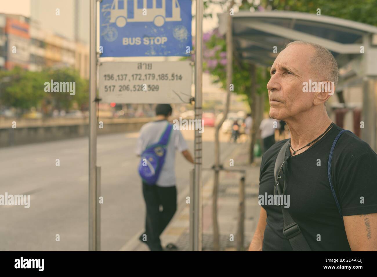 Bald senior tourist man thinking while waiting at the bus stop in ...