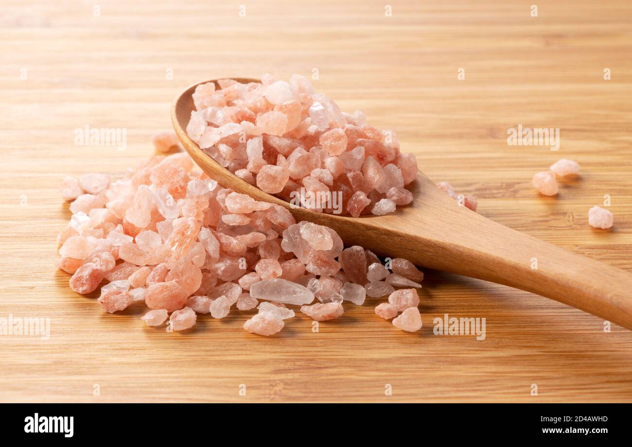 Angled shot of pink rock salt in a wooden spoon placed on a wooden ...