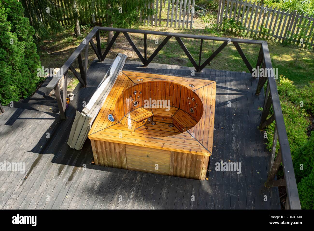 Outdoor wooden bath tub on terrace in private garden. Green trees and ...