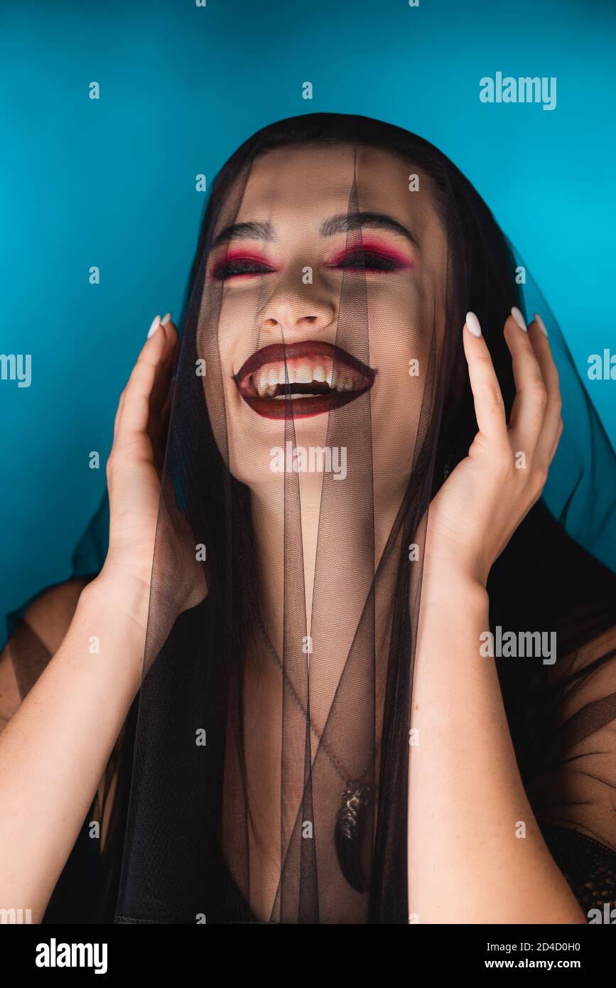 evil woman with black makeup, closed eyes and veil laughing on blue ...