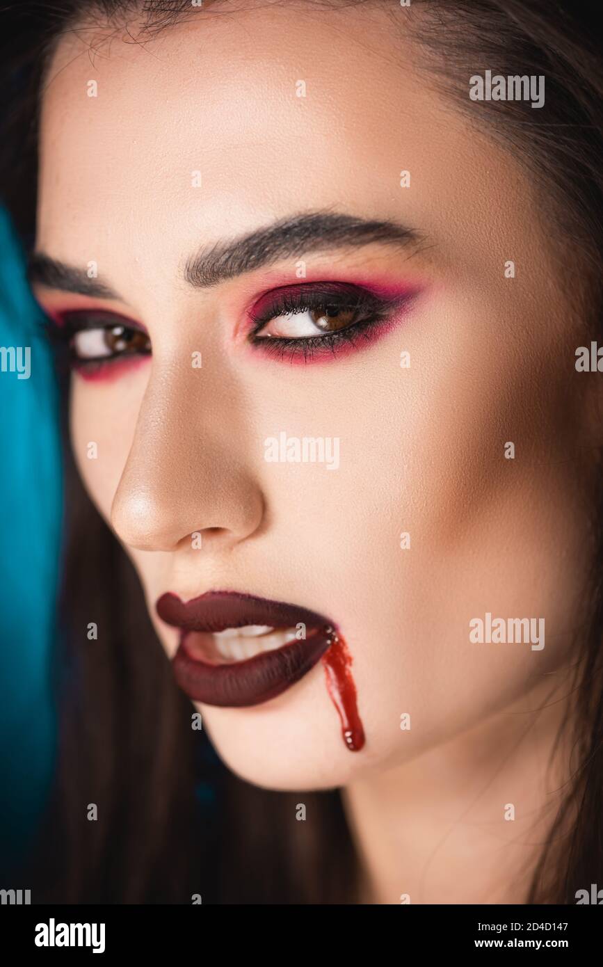 close up of creepy woman with blood on face looking at camera on blue ...