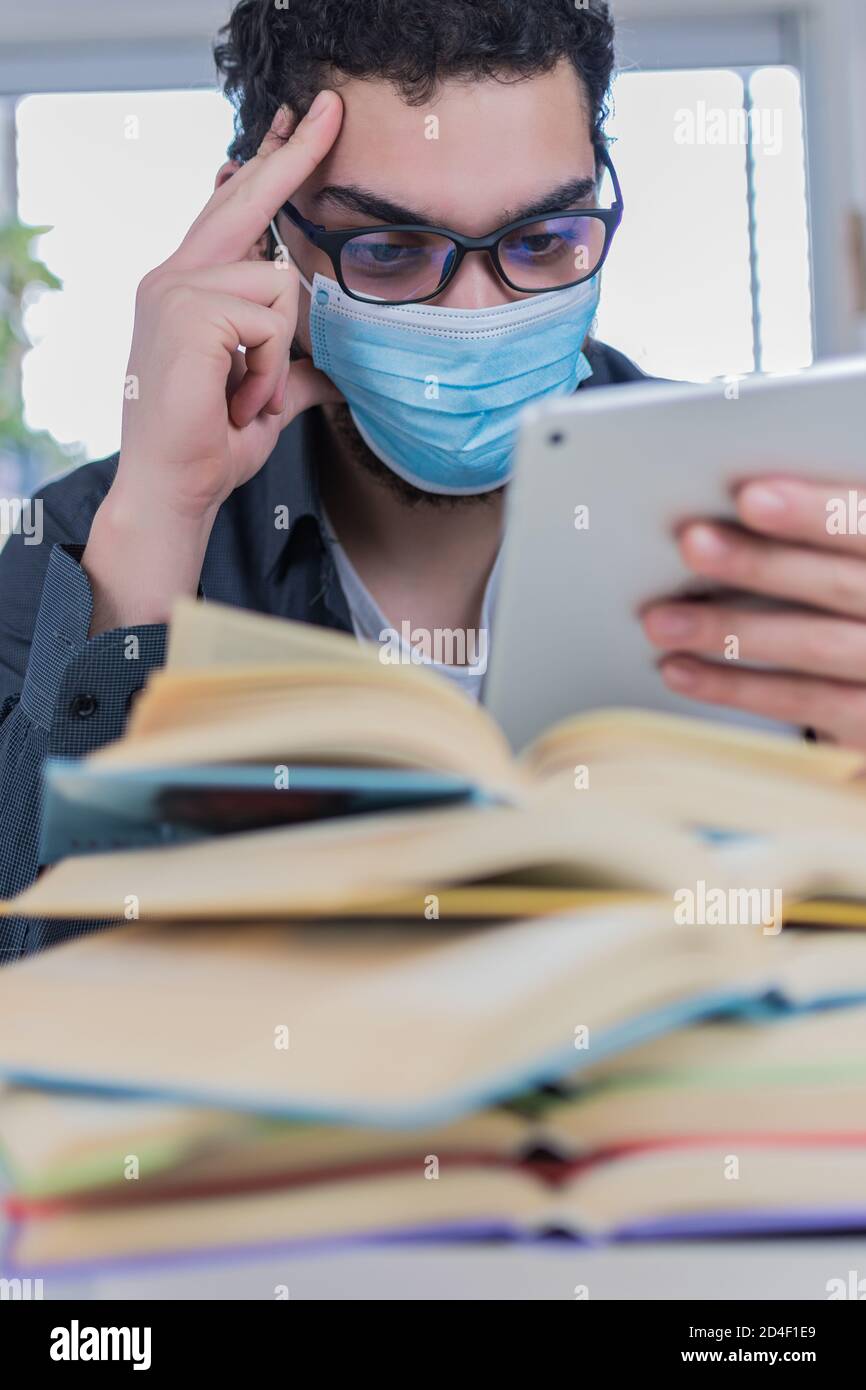 Concentrated student, wearing a protective mask studying from home ...