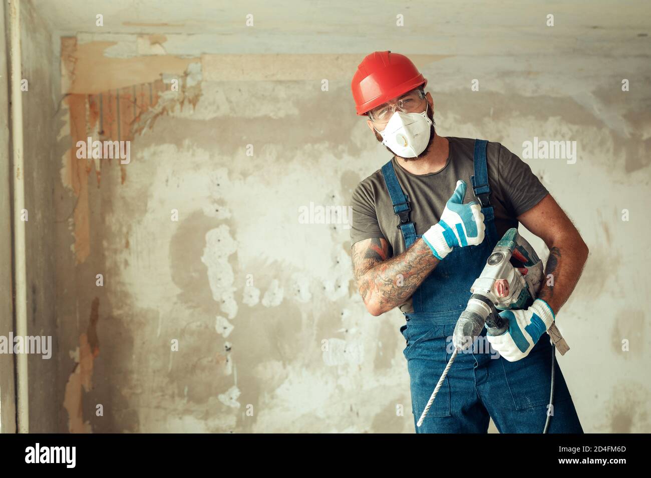 a builder with a perforator poses against the background of a wall with ...