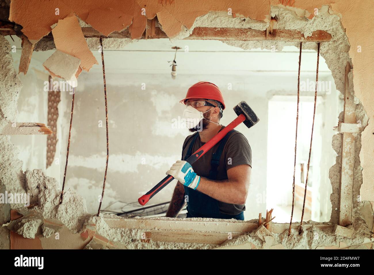 builder with a hammer in his hands breaks the cement wall The builder ...