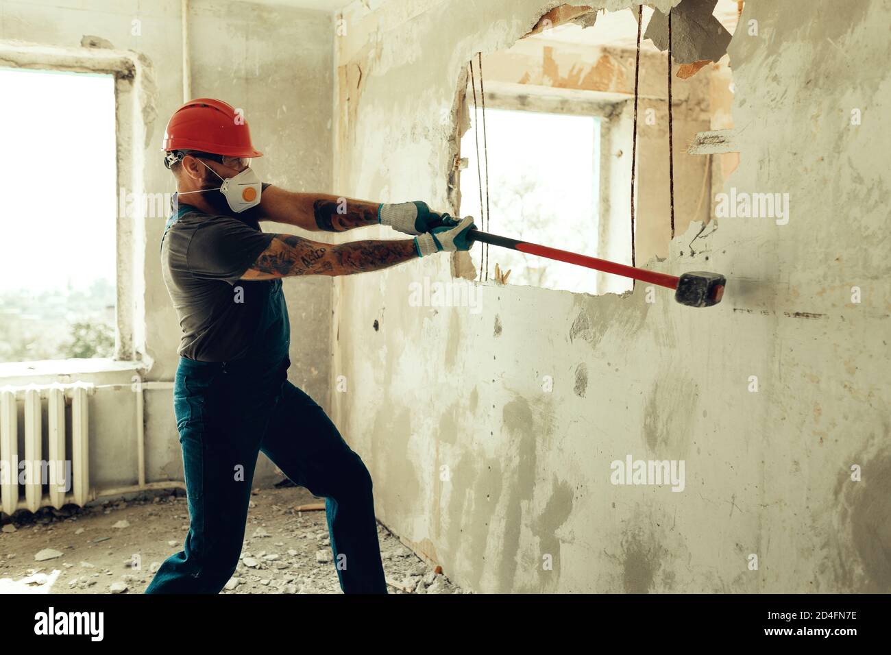 builder with a hammer in his hands breaks the cement wall The builder ...
