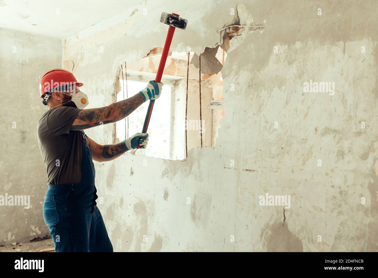 builder with a hammer in his hands breaks the cement wall The builder ...