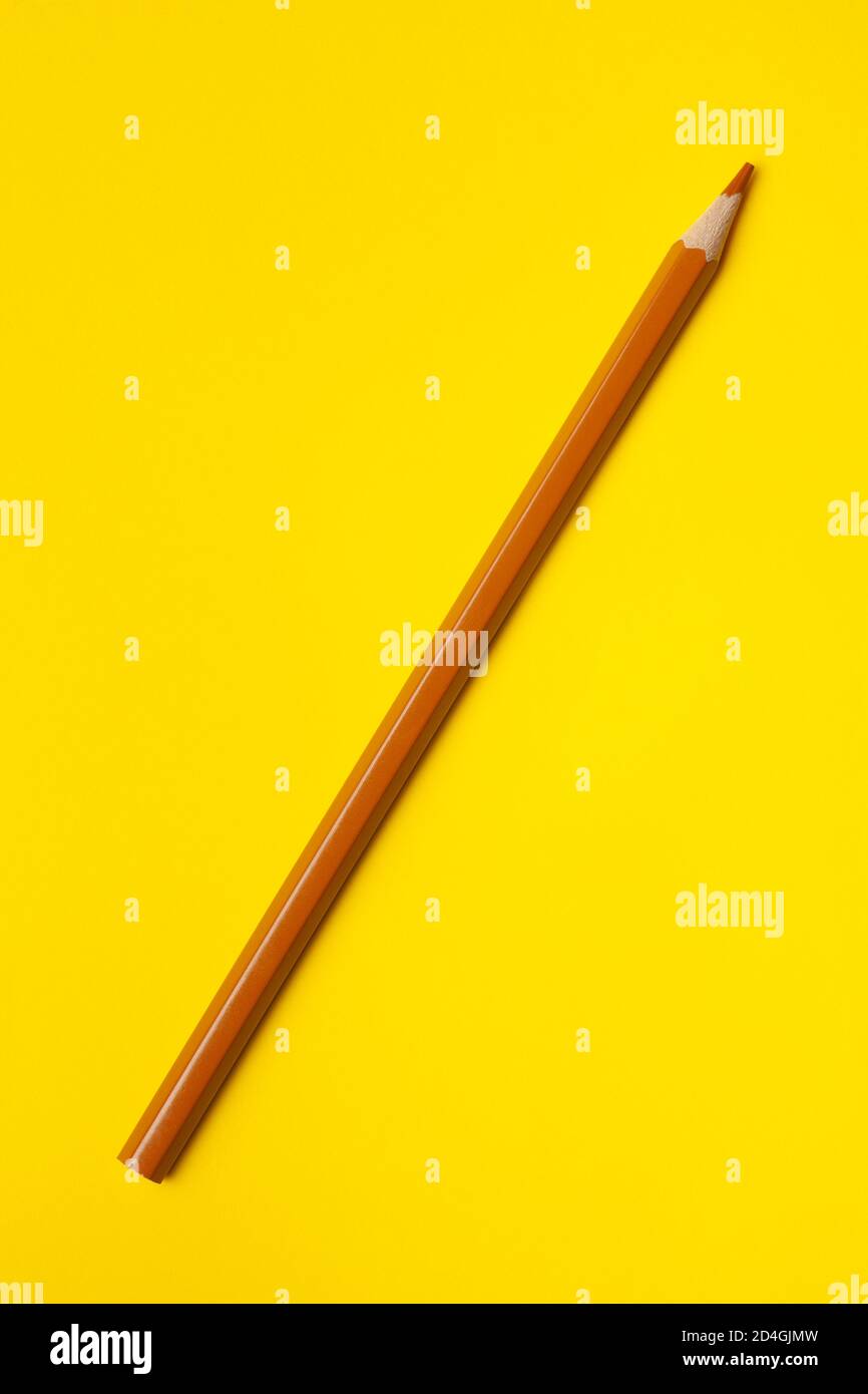 diagonal light brown sharp wooden pencil on a bright yellow background ...
