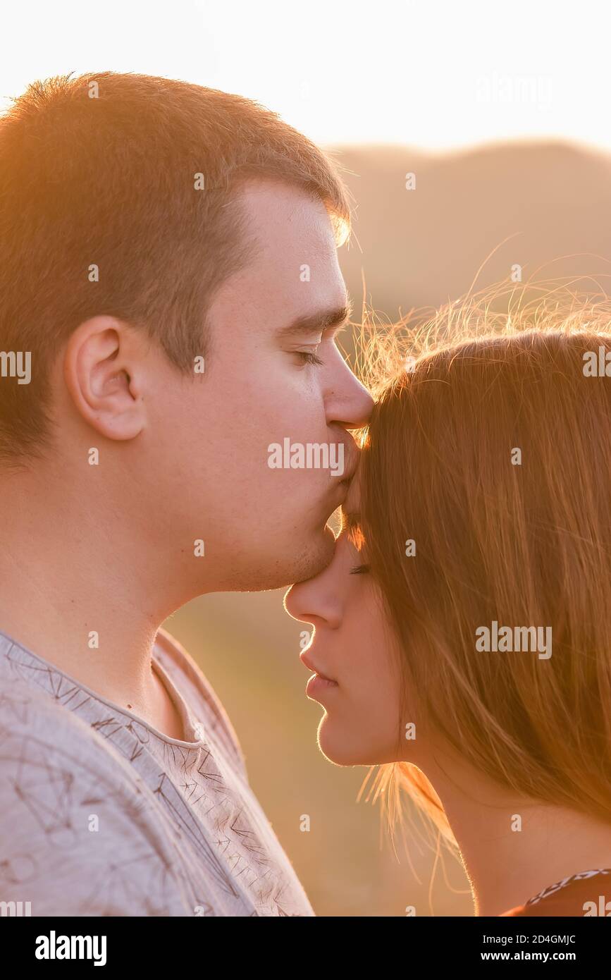 Young man kissing on the forehead of a beautiful smiling blonde girl ...