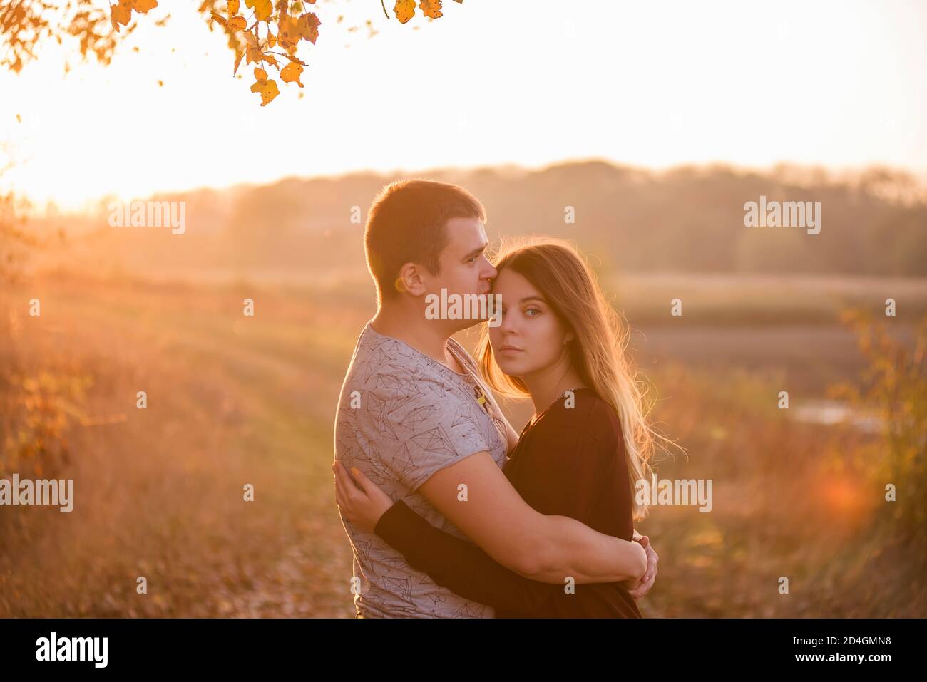 A young man kisses, hugs a beautiful smiling blonde woman with long ...