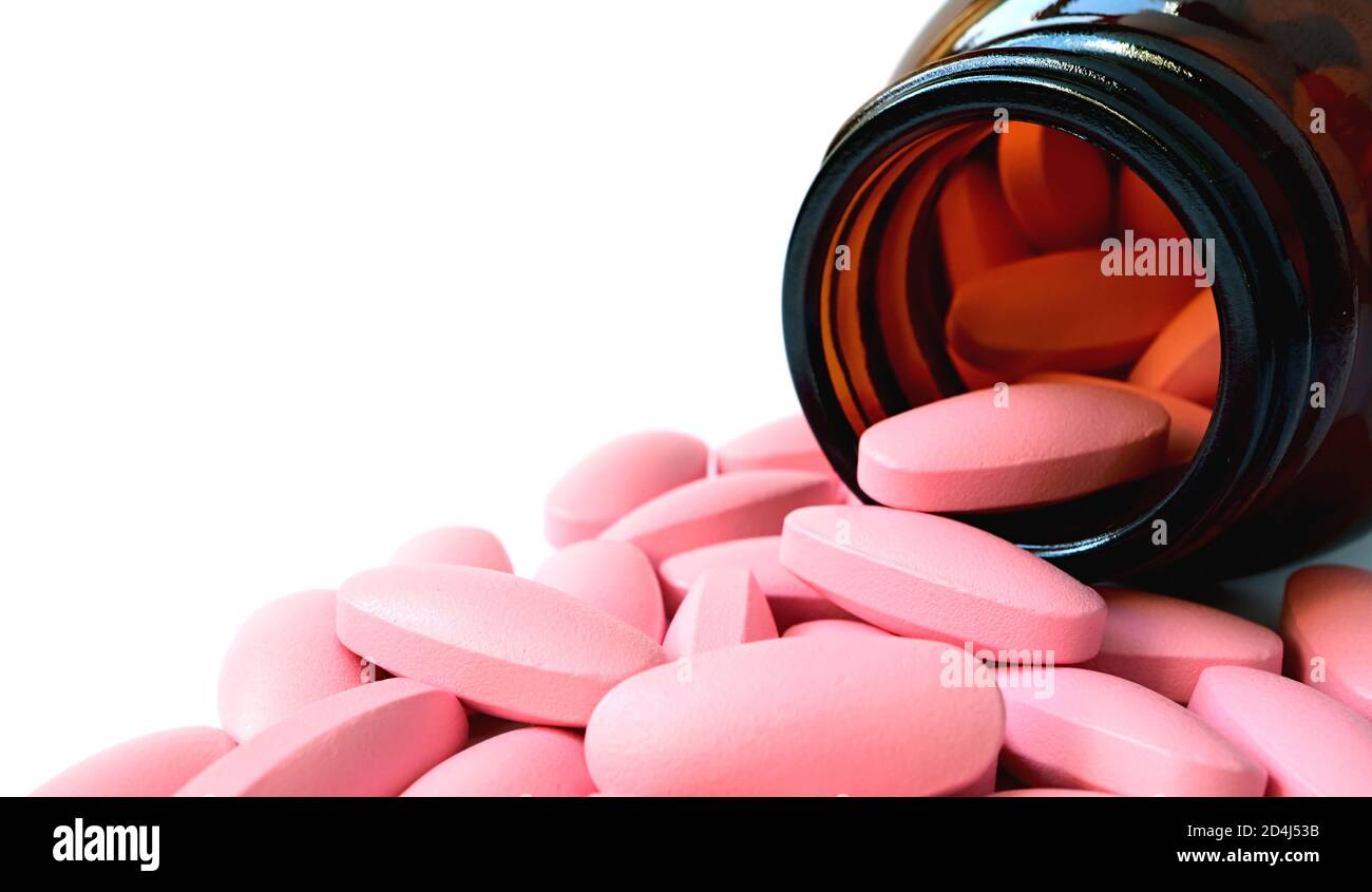 Oval shaped pink color tablets scattered from glass bottle on white ...
