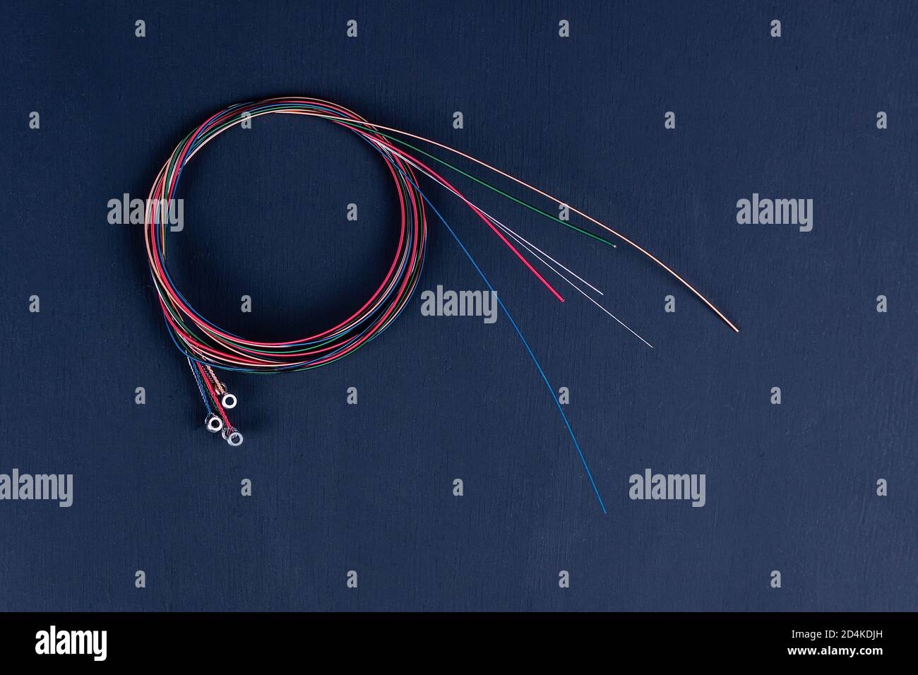 set of six coiled acoustic guitar strings randomly placed against black ...