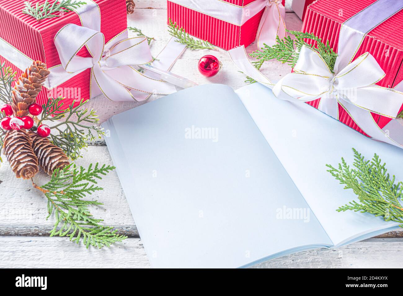 Female hand writing in notepad with christmas decoration and gift boxes on white wooden table ...