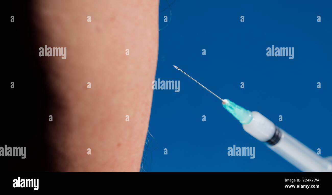Closed syringe isolated on blue background, with man's arm Stock Photo ...