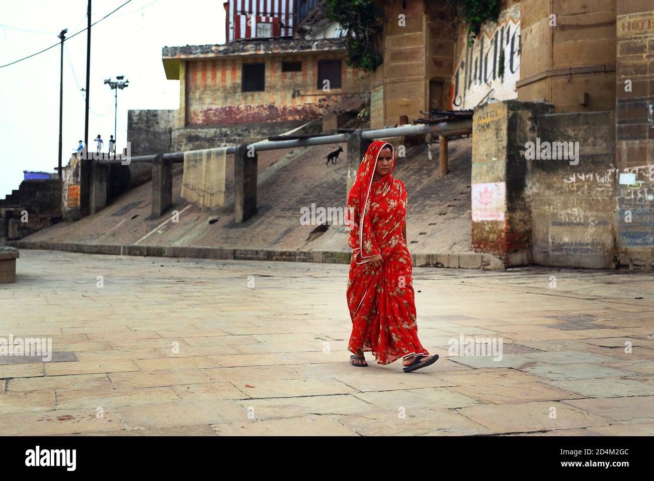 A woman wearing a red dress walks by the Ganges river in Varanasi, Ind ...