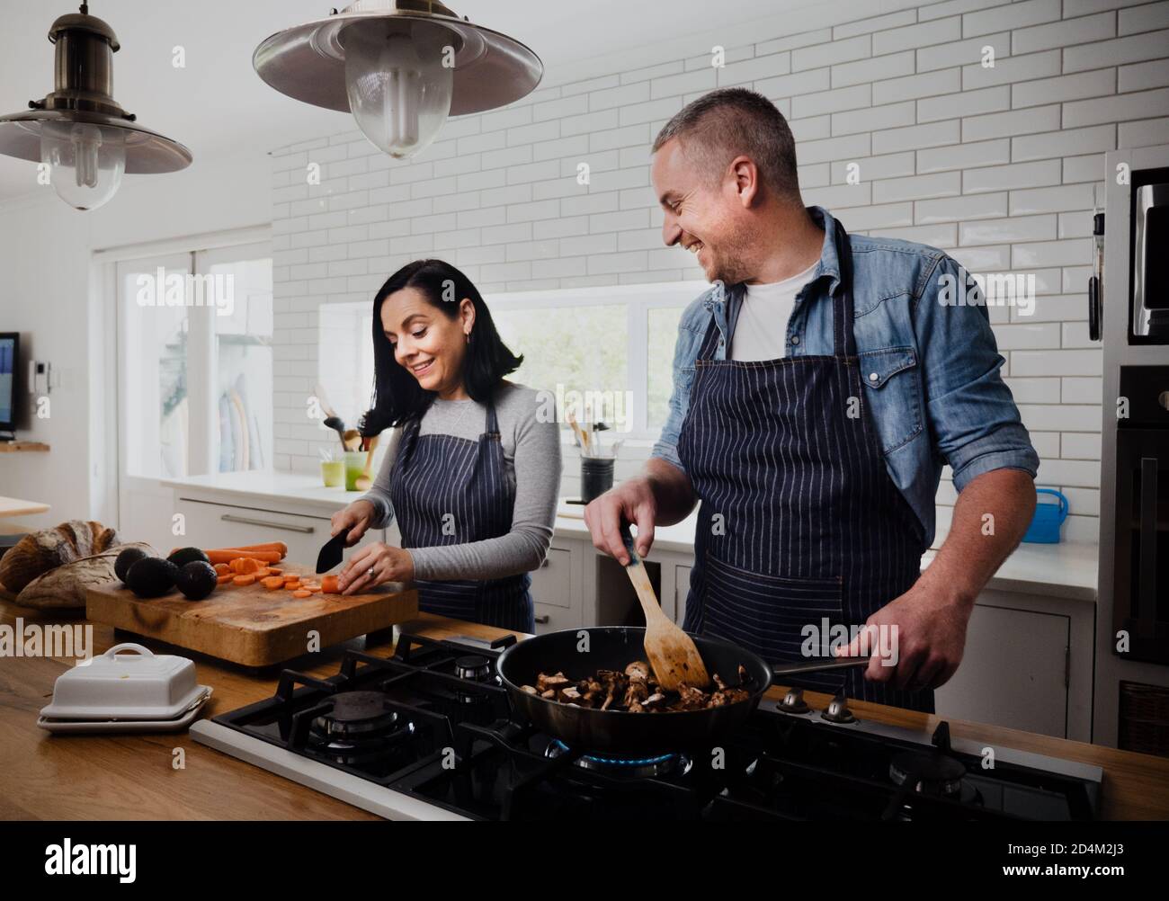 Caucasian husband and wife cooking together in the kitchen, smiling and ...