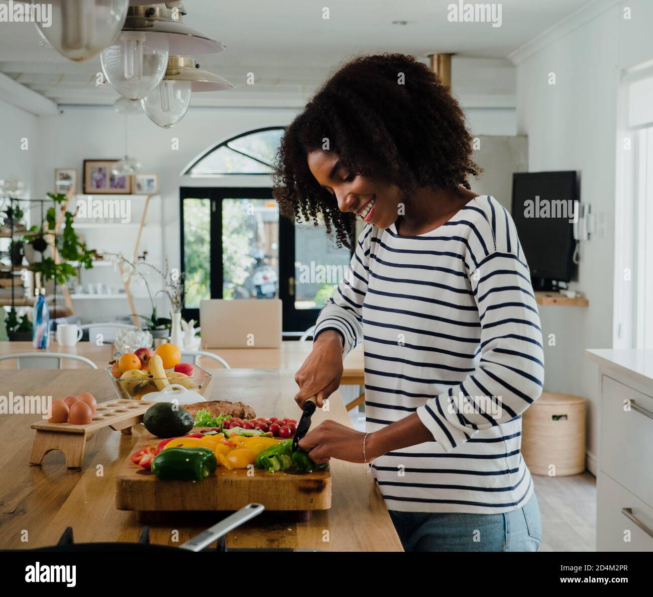 Young woman chopping vegetables in kitchen at home, happy and smiling ...
