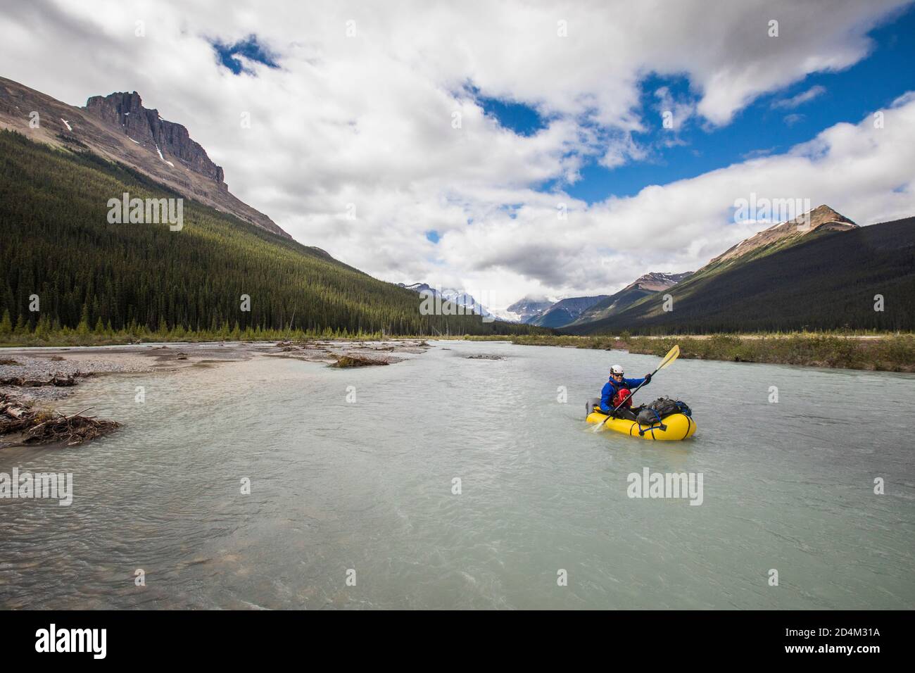 Man paddling raft on river through vast rocky mountain valley Stock ...