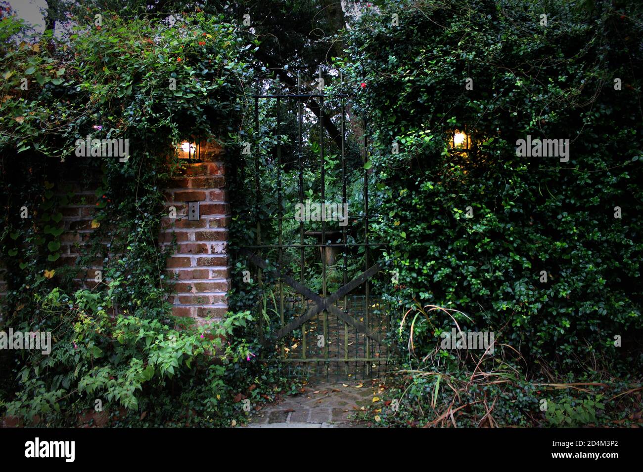 a mysterious metal garden gate with two lamps on an old weathered brick ...