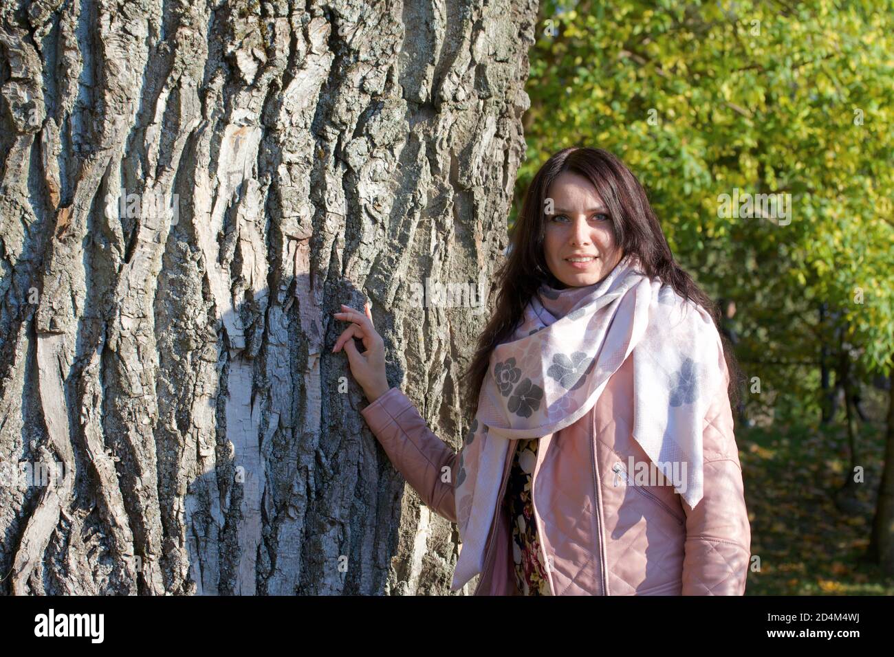 Girl near an old tree in an autumn park. She put her hand on the barrel ...