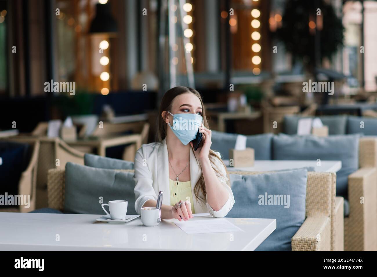 Female manager in suit and medical mask works remotely on street cafe ...