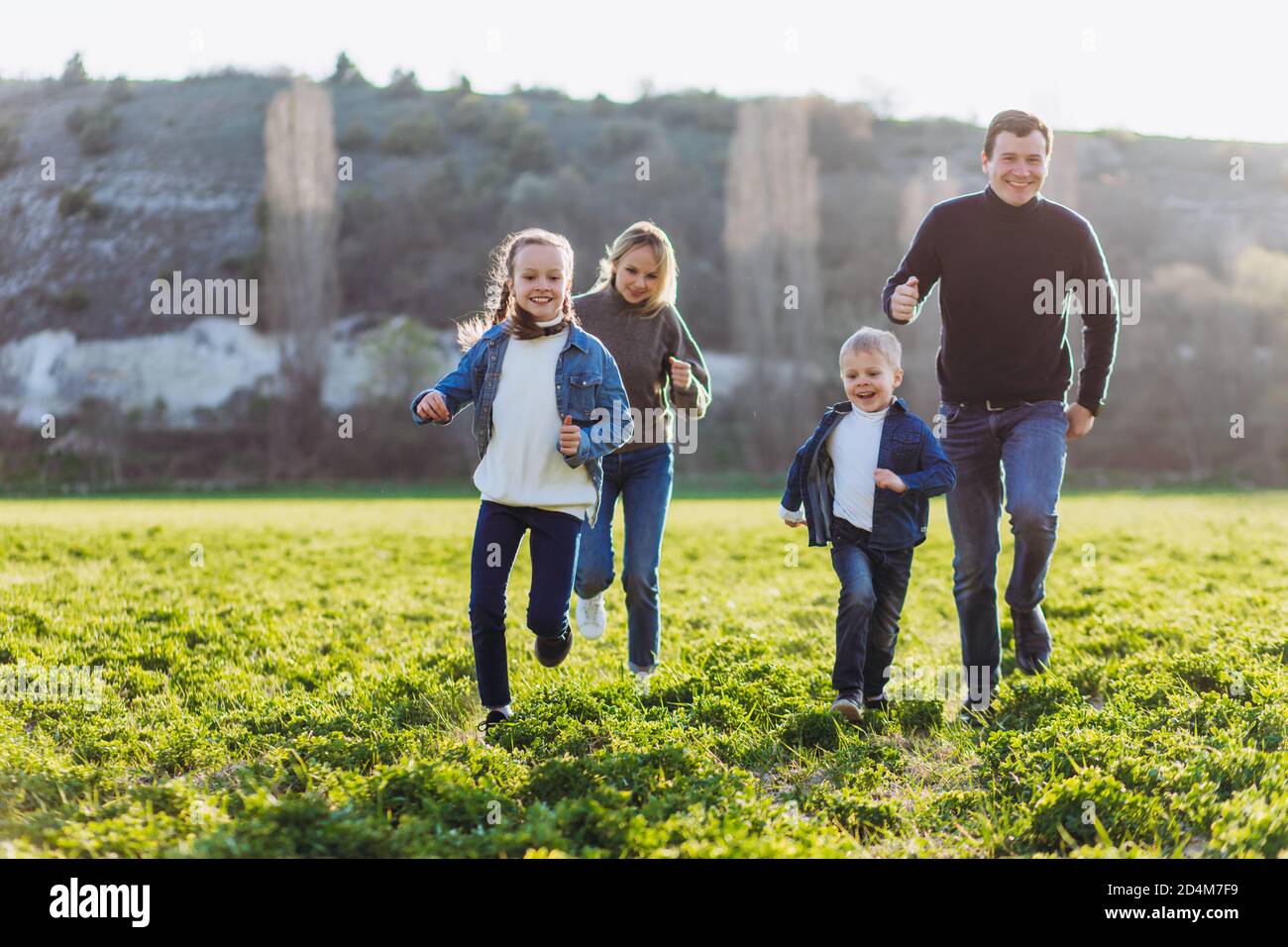 Father, mother and children run through a green field Stock Photo - Alamy