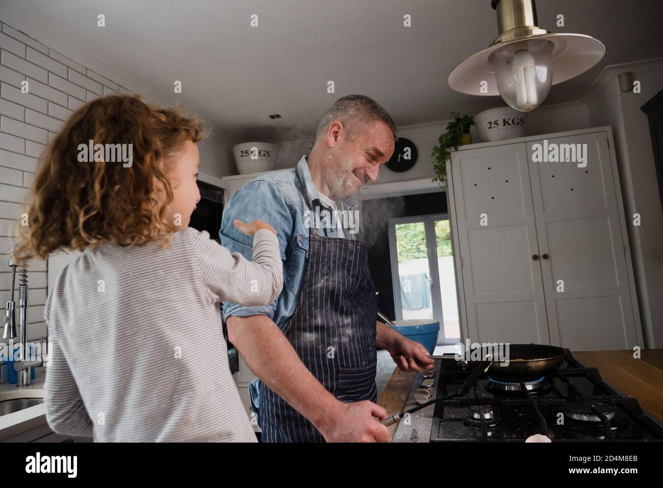 Daughter throwing flour at father, having fun in the kitchen baking ...