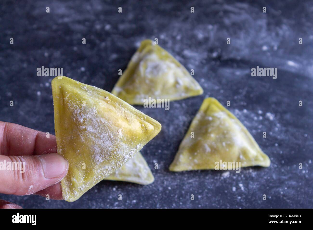 Hand holding fresh Ravioli triangle on floury dark background. Italian ...