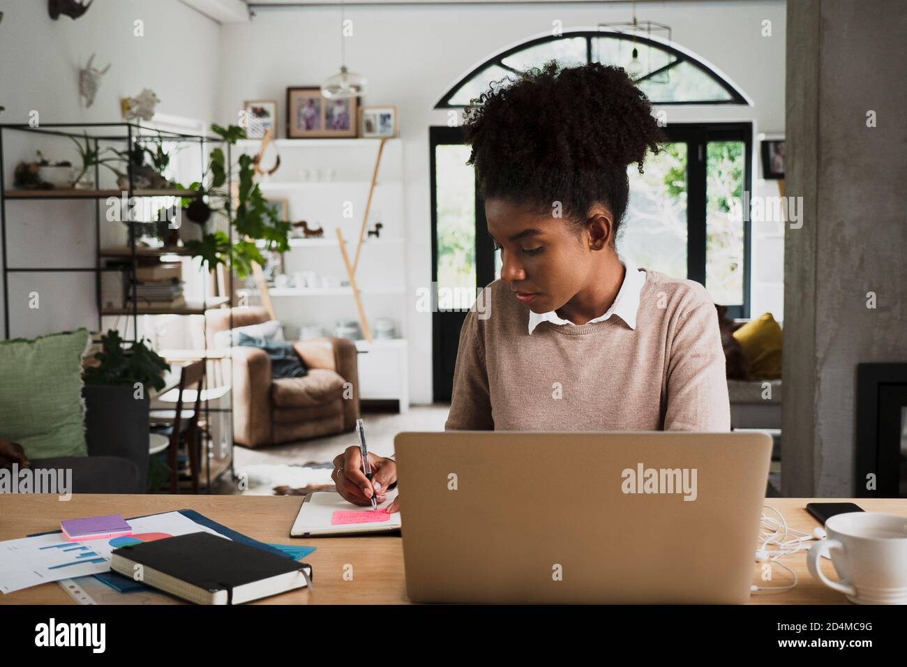 Mixed race female student studying online writing notes on notepad ...