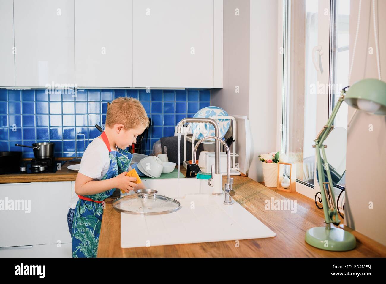 a boy in an apron washes dishes in the kitchen at home Stock Photo - Alamy